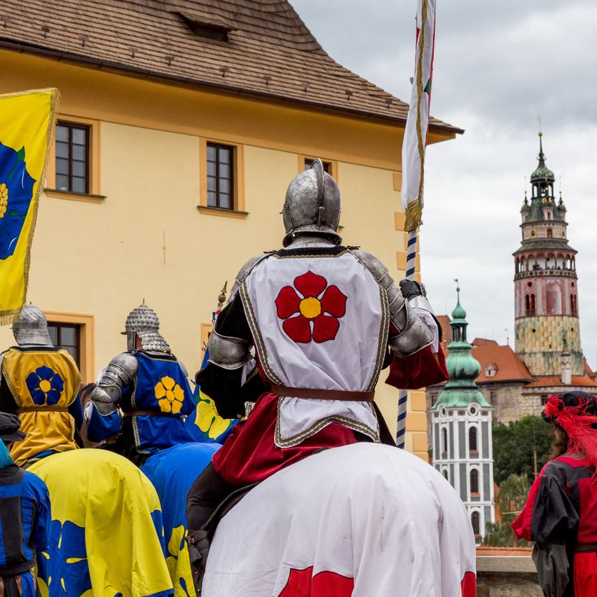 Knights in colorful armor ride horses in a medieval town square. A ...